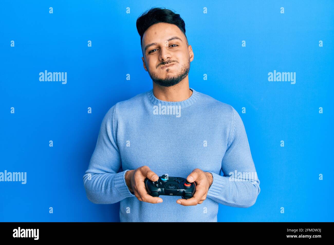 Young arab man playing video game holding controller puffing cheeks ...