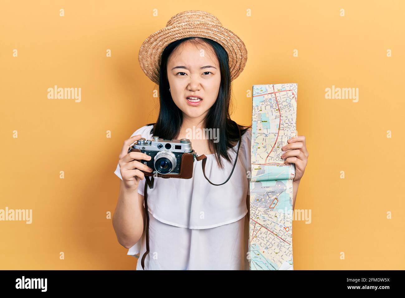 Young chinese girl holding city map and vintage camera clueless and ...