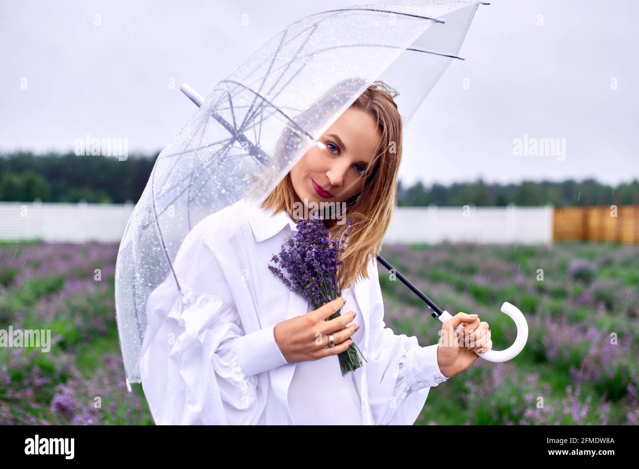 Young woman holding umbrella on stormy weather, standing in open field ...