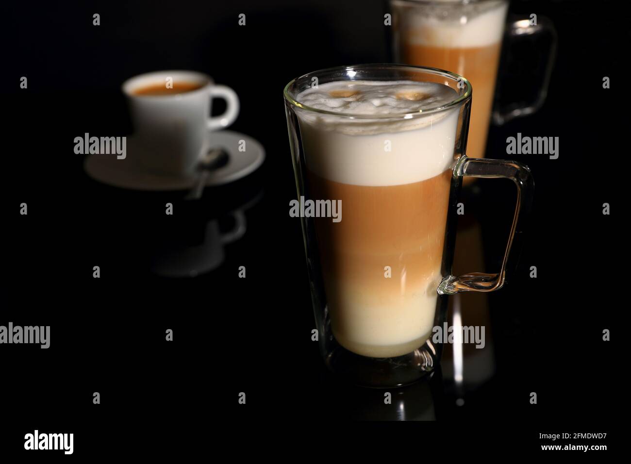 A glass of late coffee and a cup of espresso on a black background ...
