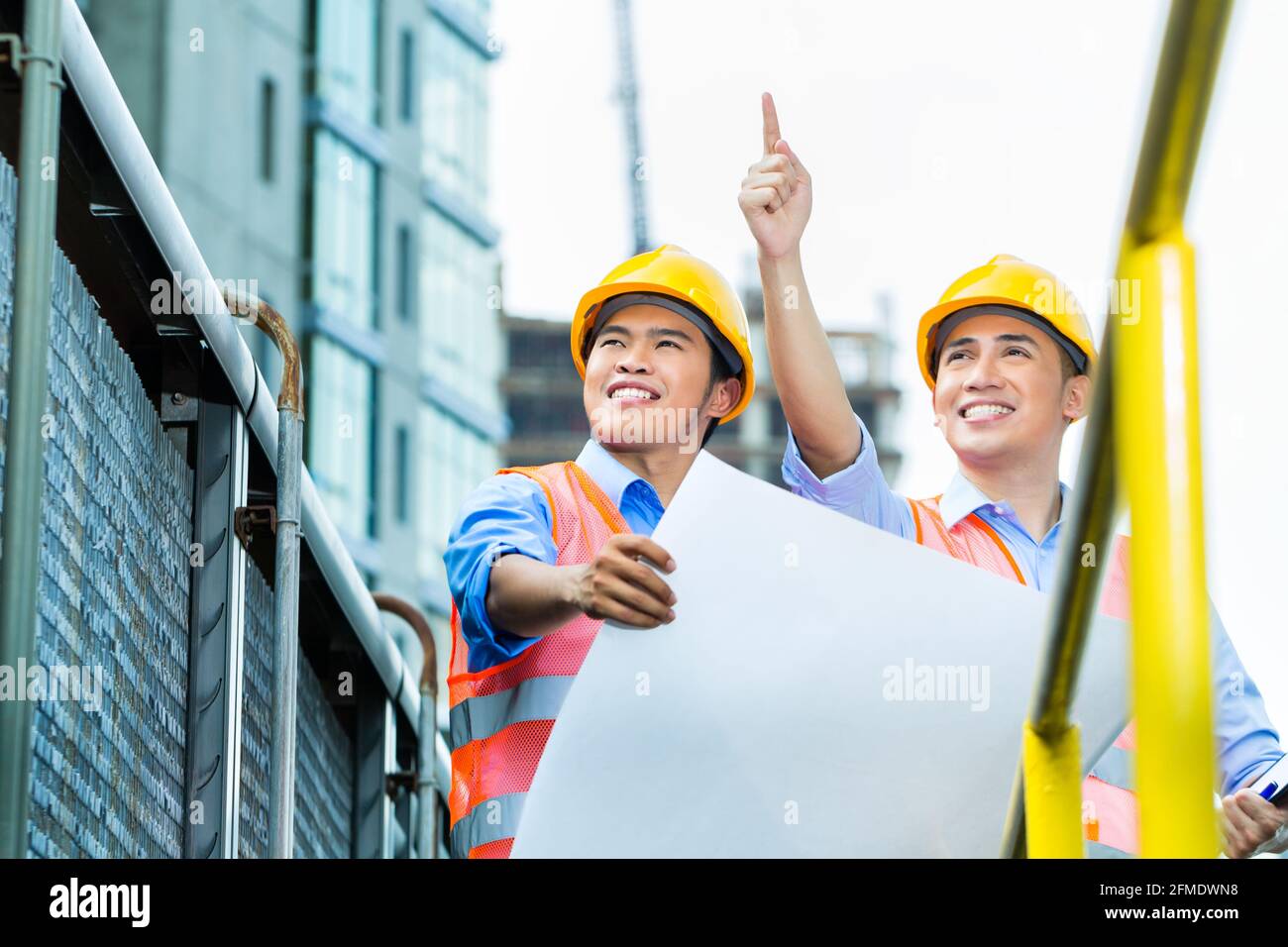 Asian Indonesian construction workers with blueprint or plan on ...