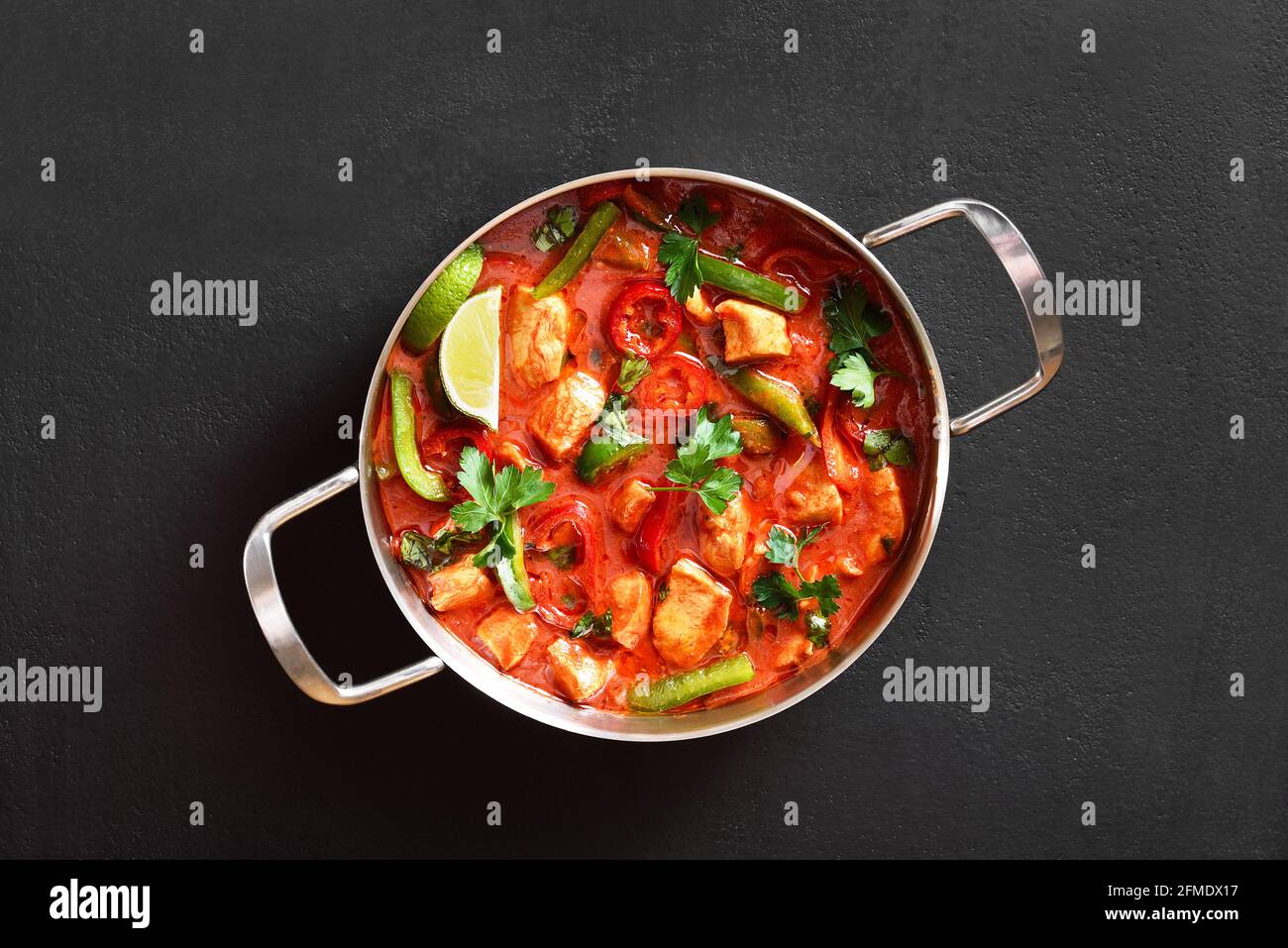 Thai style red chicken curry with vegetables in pan over black stone ...