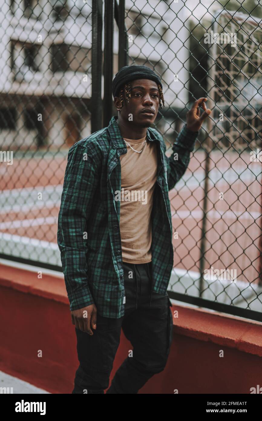 Handsome and stylish Spanish man touching the chain-link fence and ...