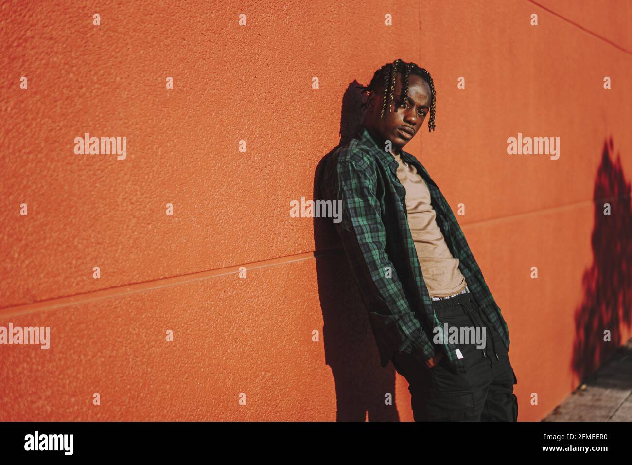 Handsome stylish Spanish man leaning on a red wall and posing with a ...
