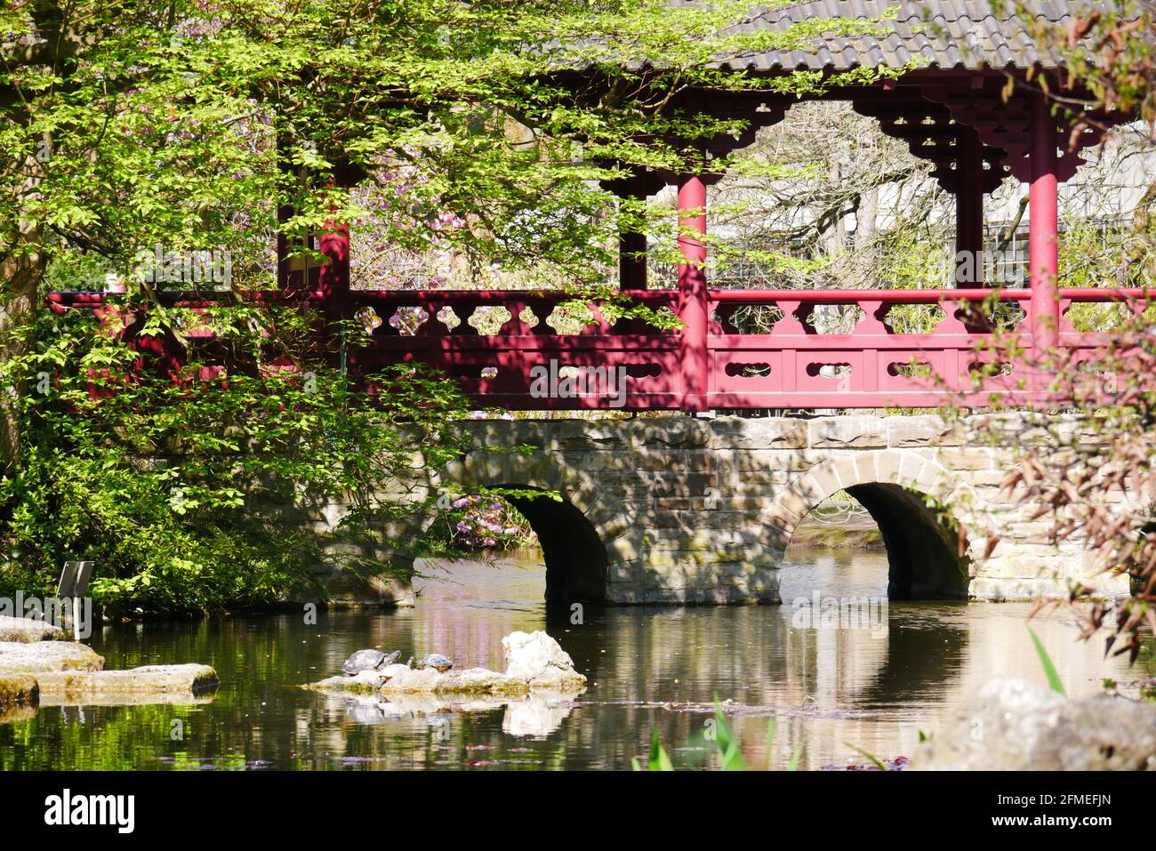 covered japanese stone bridge with red wooden railings in the sunlight ...