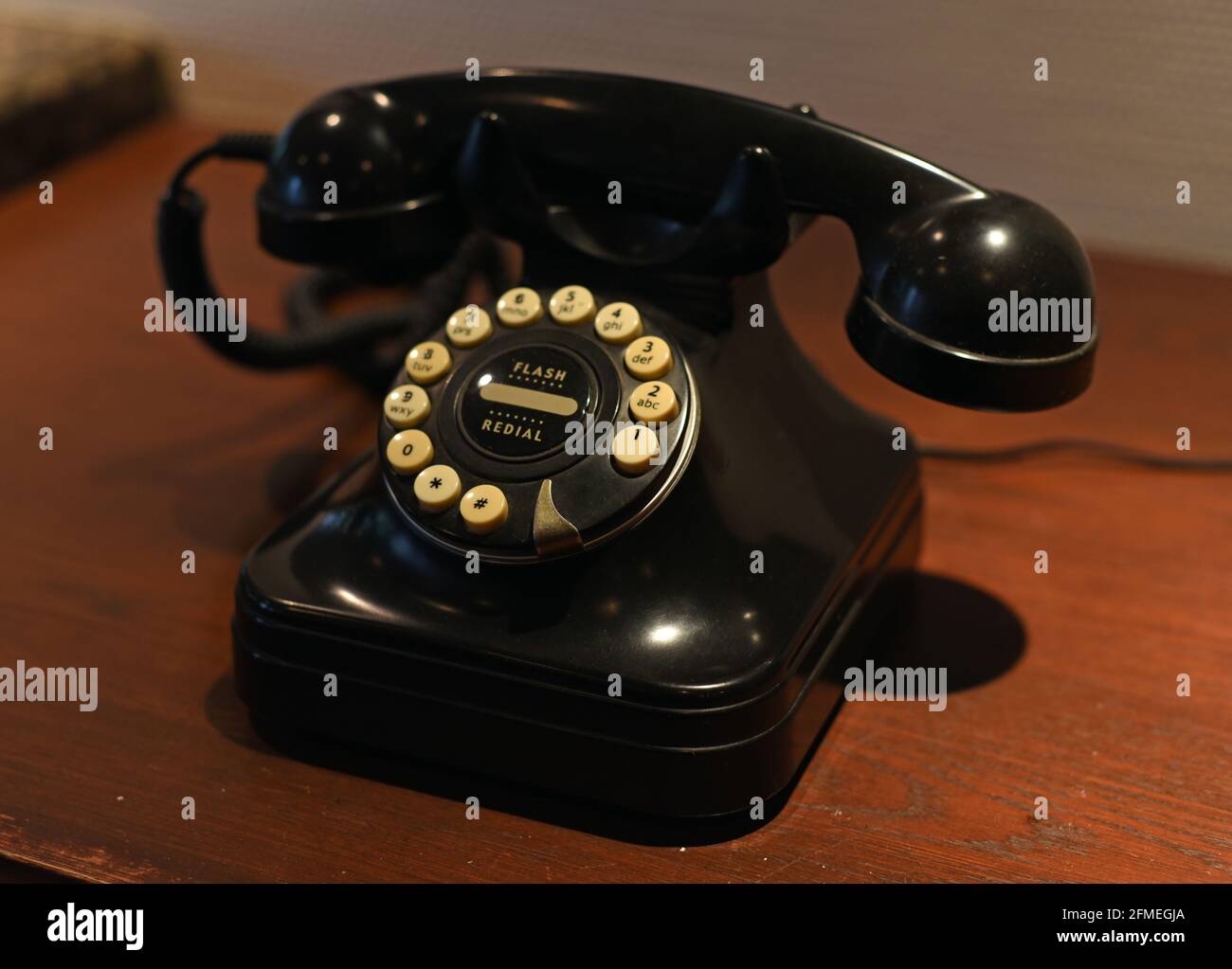 An old black rotary push button dial telephone sits on a wooden counter ...