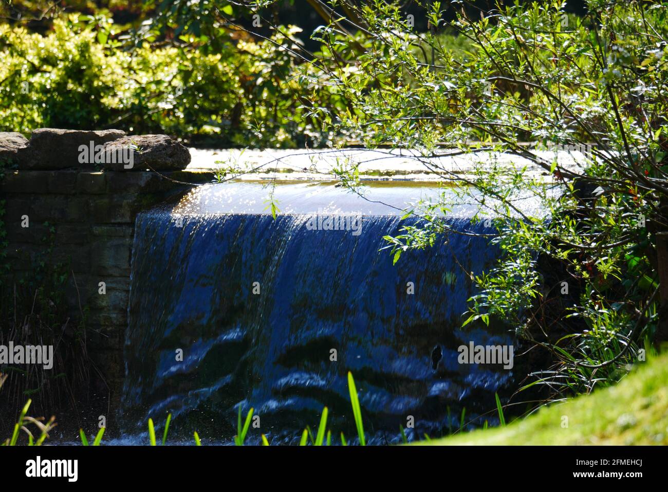 shimmering blue waterfall in spring at a dam made of old stone bricks ...