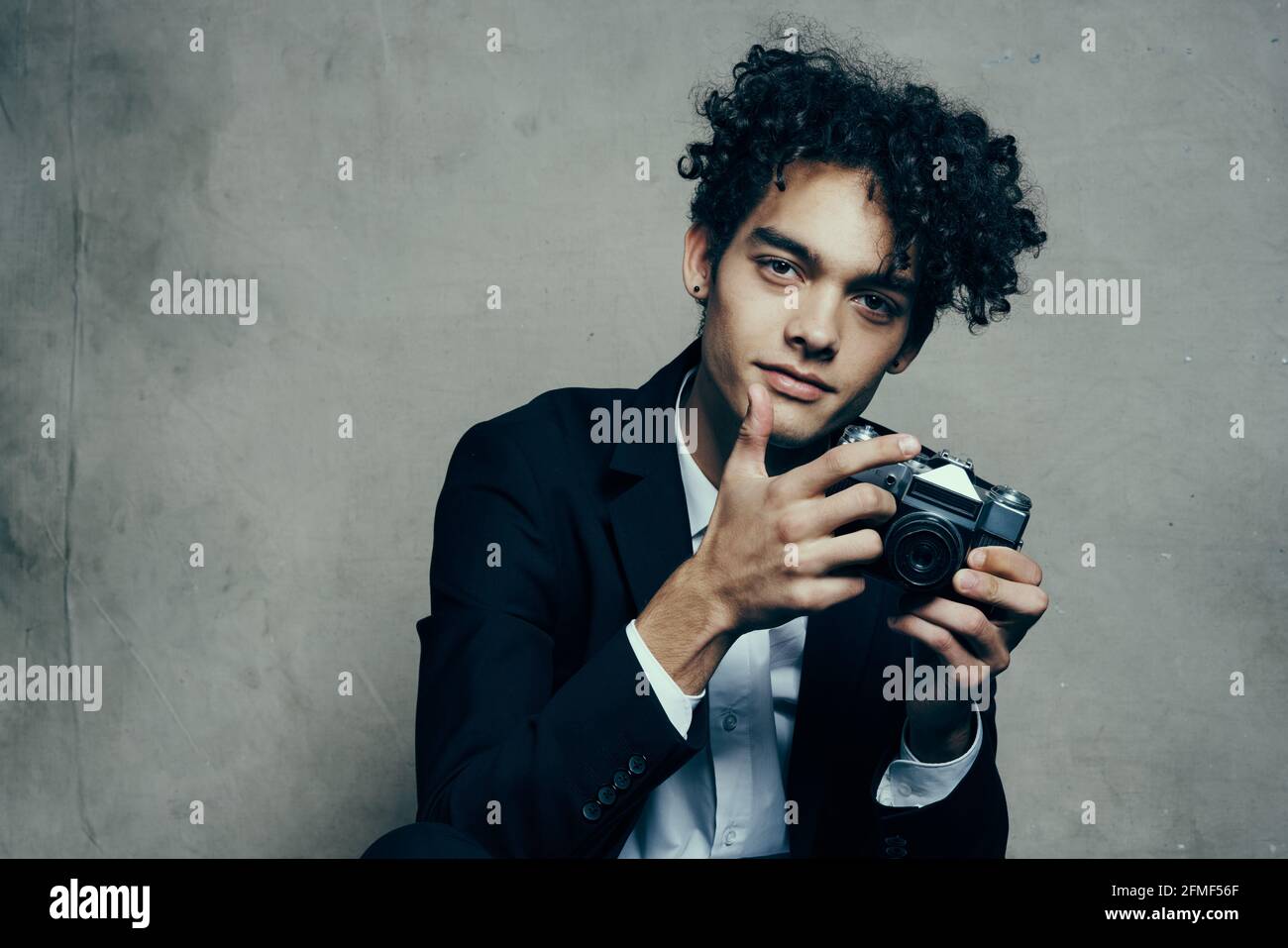 curly-haired man in a classic suit looks at the camera in his hand ...