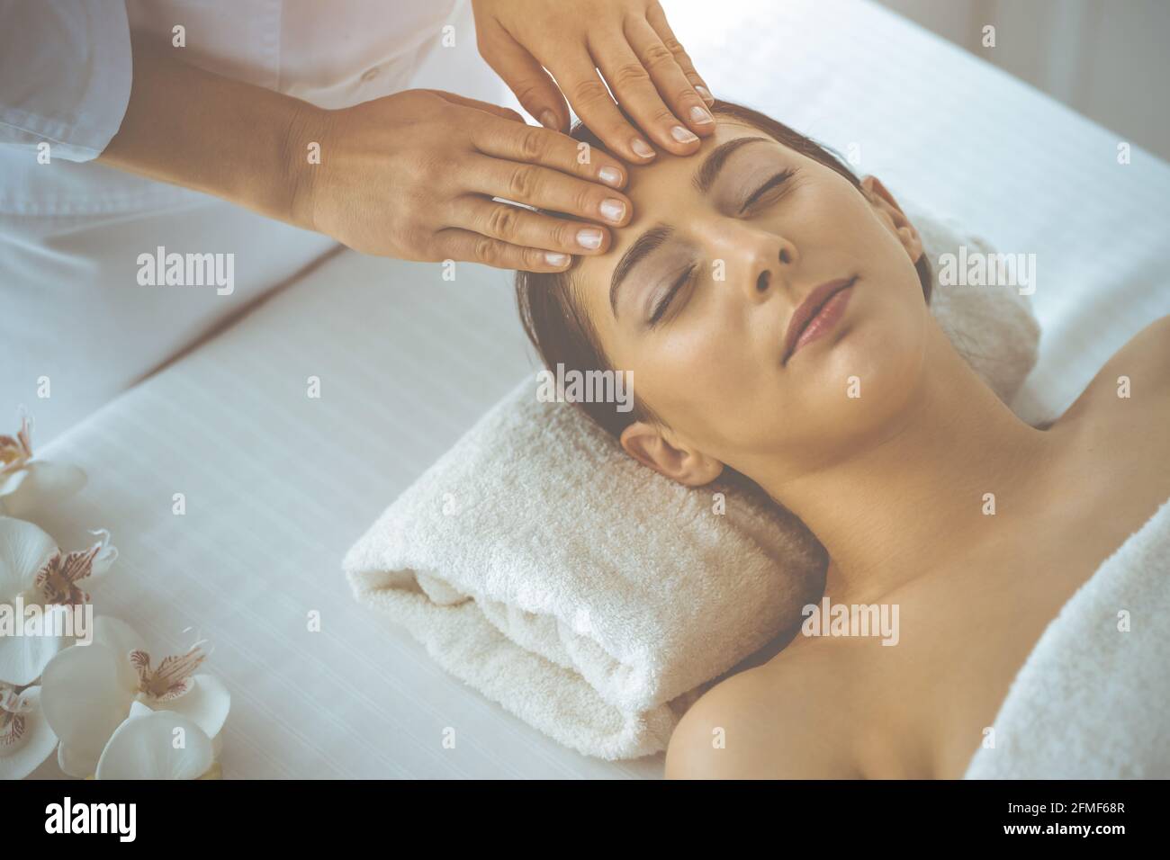 Beautiful brunette woman enjoying facial massage with closed eyes in ...