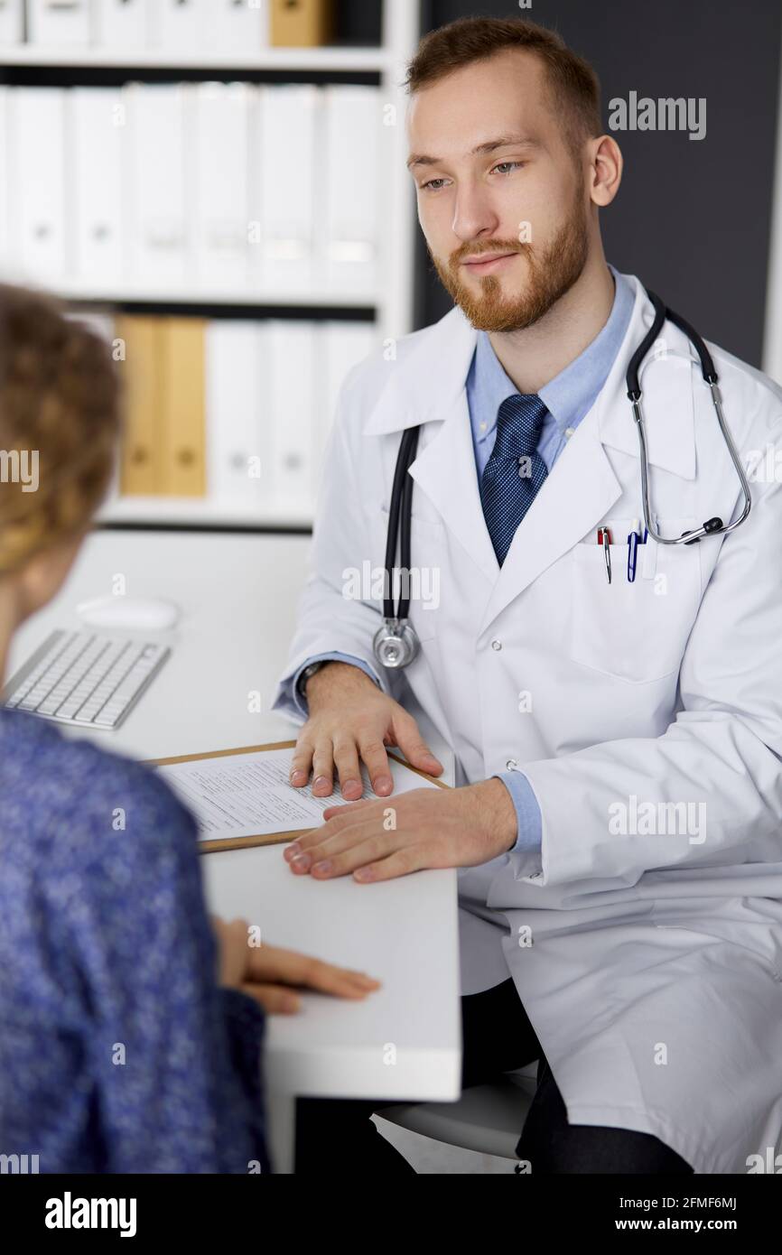 Friendly red-bearded doctor and patient woman discussing current health ...