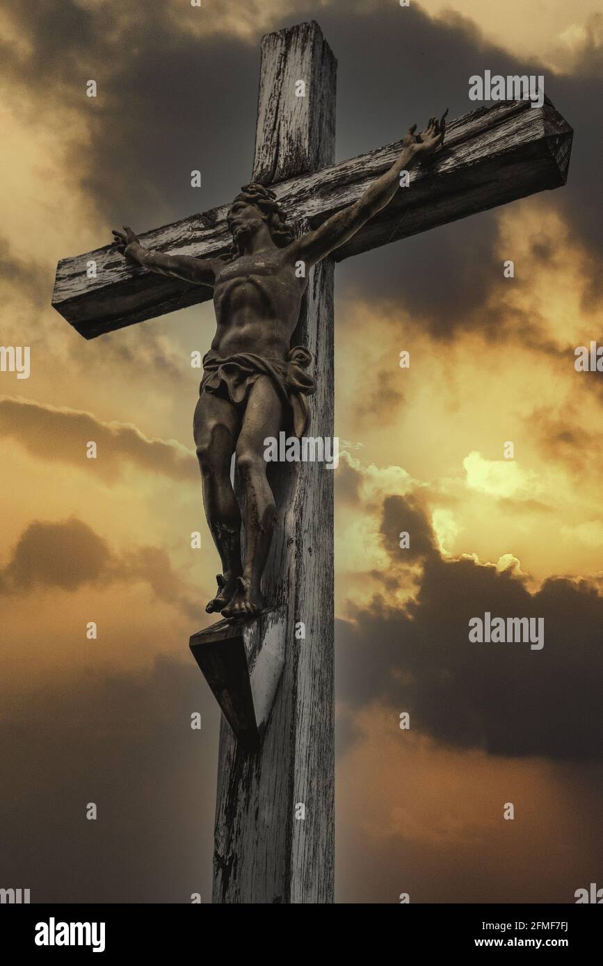 A vertical shot of a crucifix with cloudy sky at sunset in the ...
