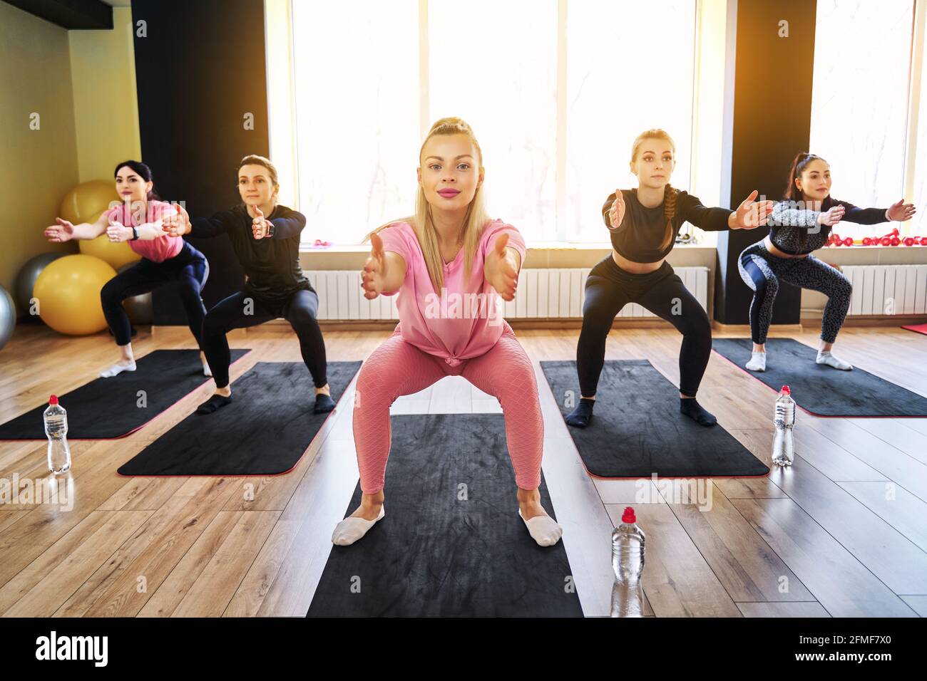 Young woman doing squat exercise at group fitness training with other ...