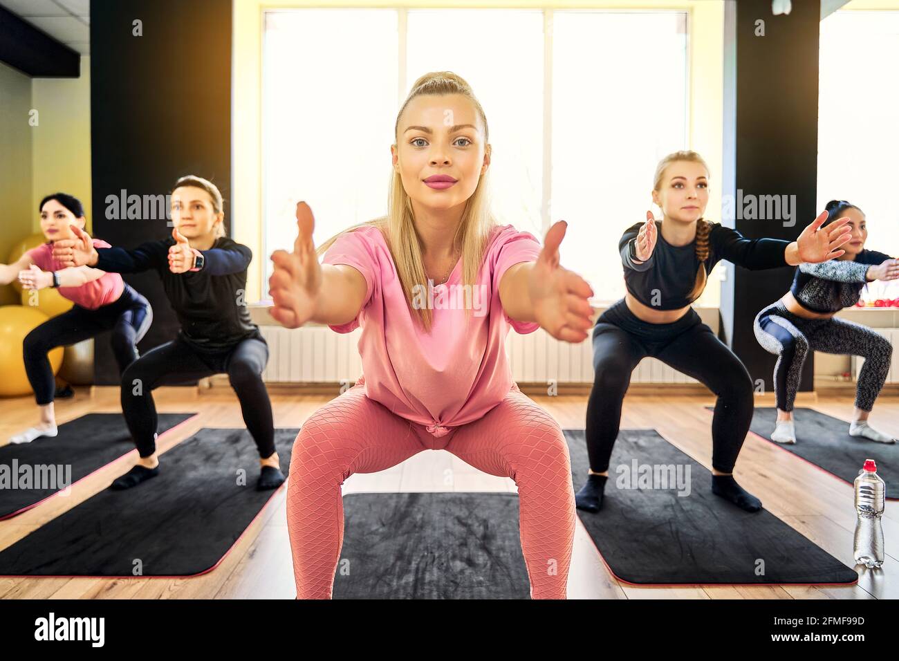 Young woman doing squat exercise at group fitness training with other ...