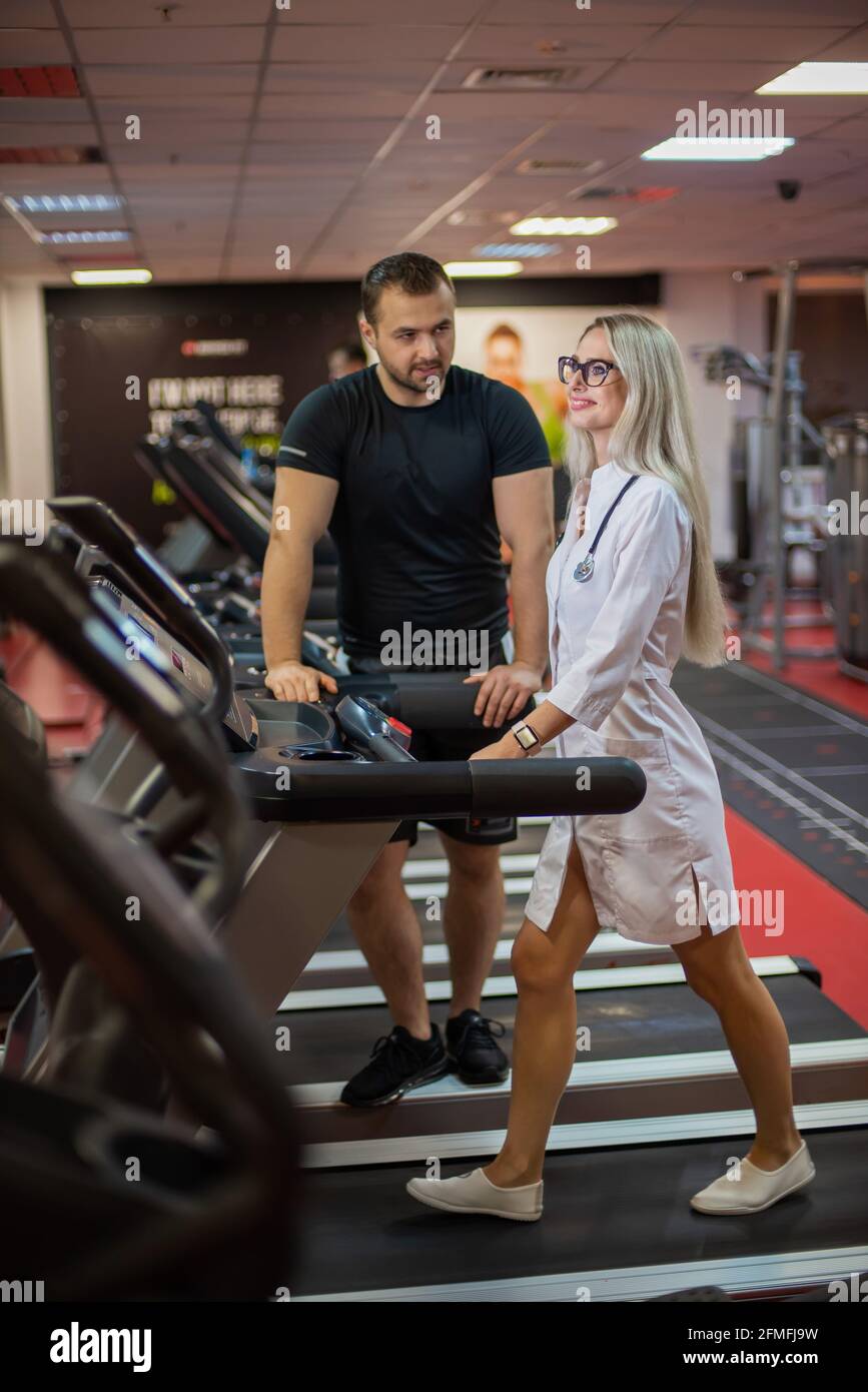 The athlete in the gym controls the treadmill exercises of a beautiful ...