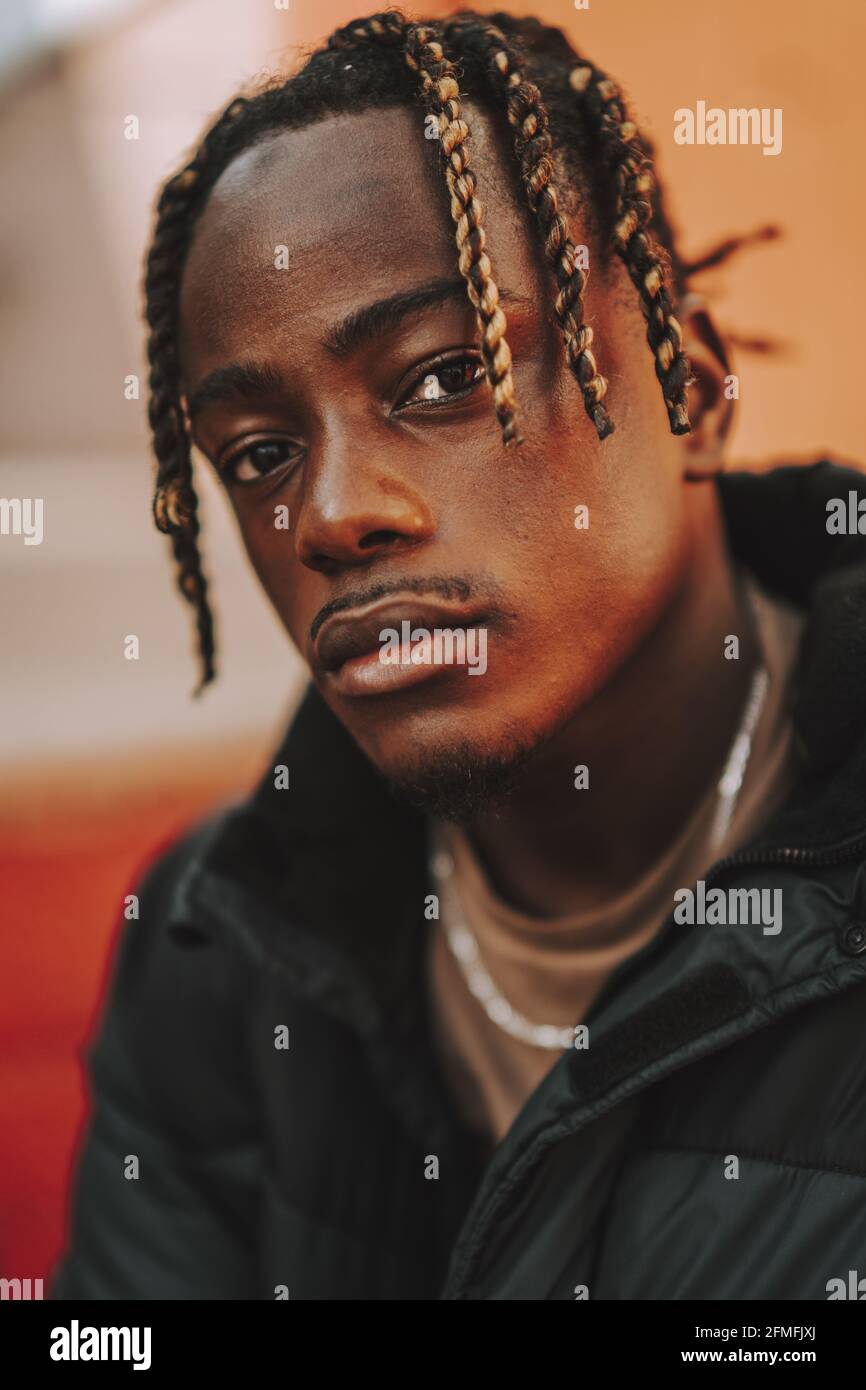 A handsome stylish Spanish man with dreads posing on a red blurred ...