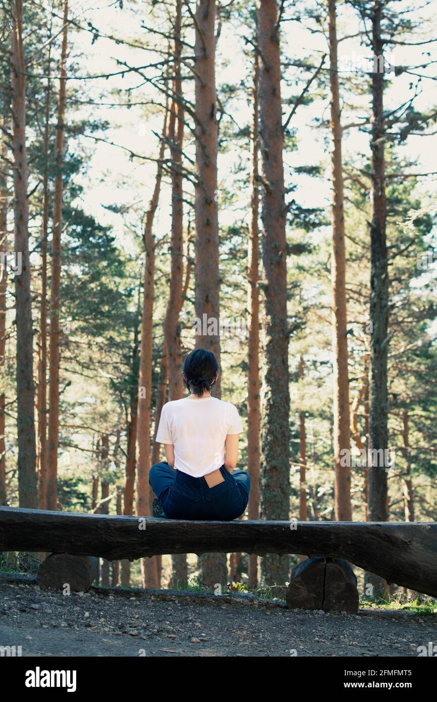 Young woman sitting with her back to an untreated wooden bench against ...