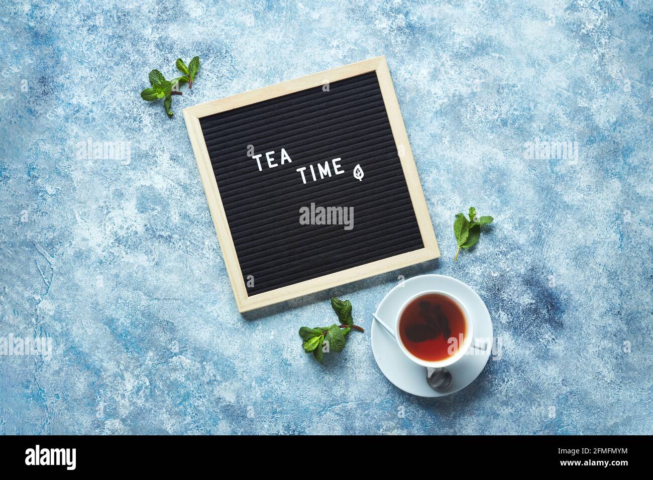 Tea time. Black letter board with text on blue table with glass cup of ...