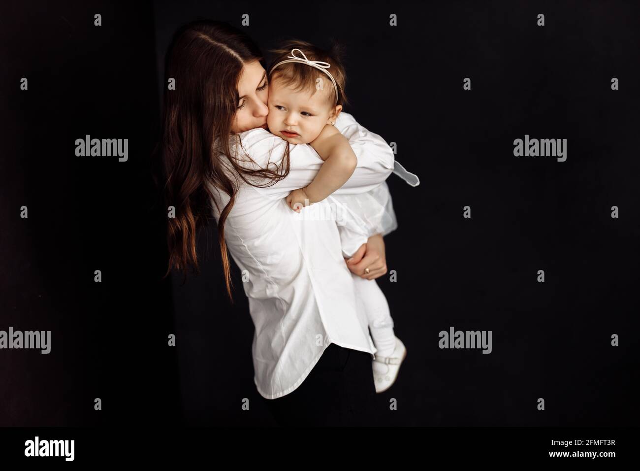 Dark-haired young mother gently holds in her arms and hugs little ...