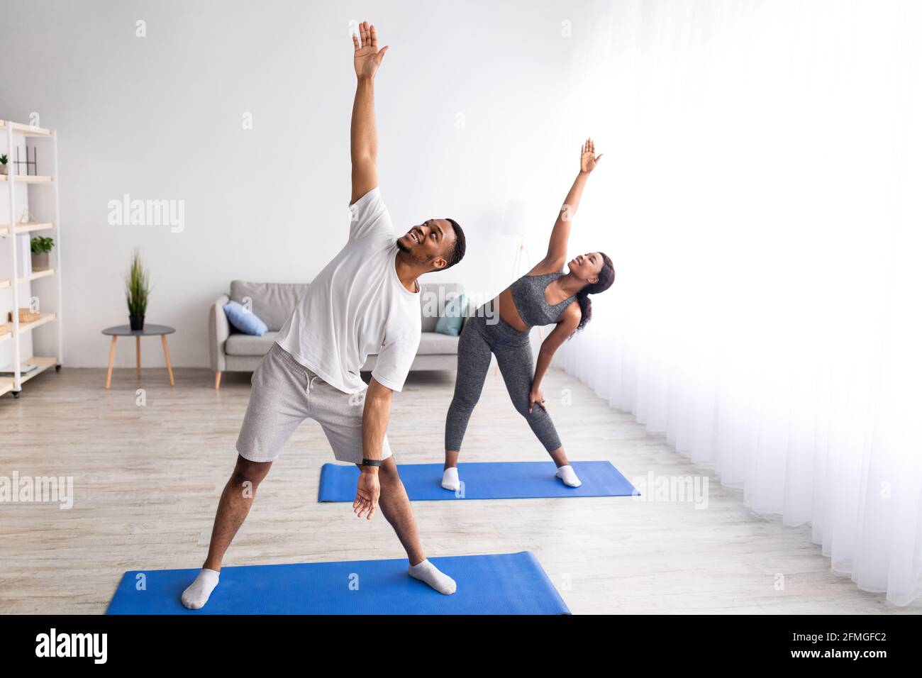 Young black couple practicing yoga at home, standing in triangle pose ...