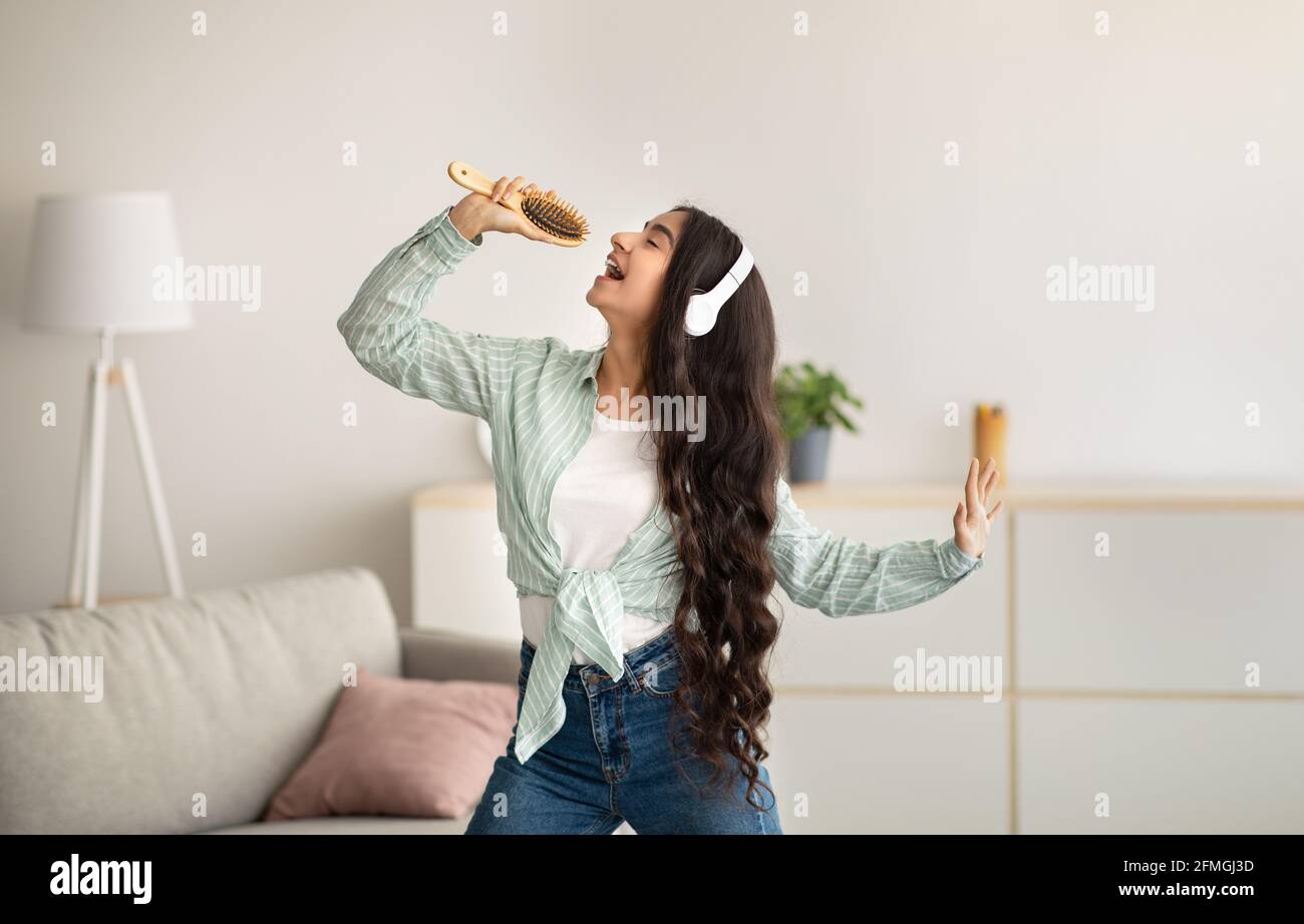 Cheerful Indian woman with hairbrush as mic singing her favorite song ...