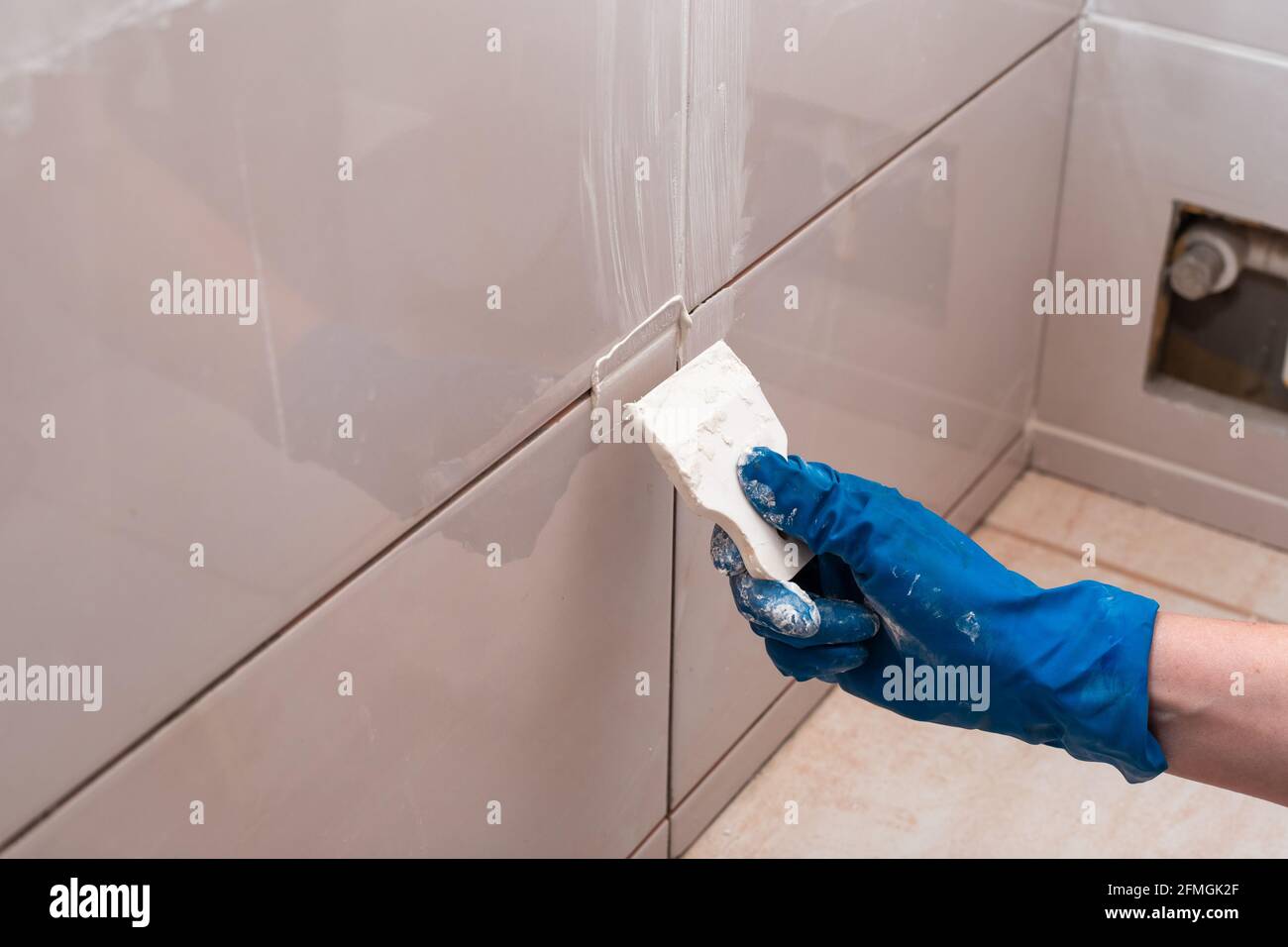 Repair and wall cladding with tiles. The master rubbing the tile joints ...