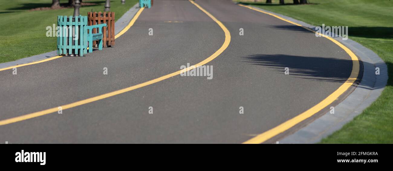 Bicycle path through the park. Asphalt for walking and a bench for ...