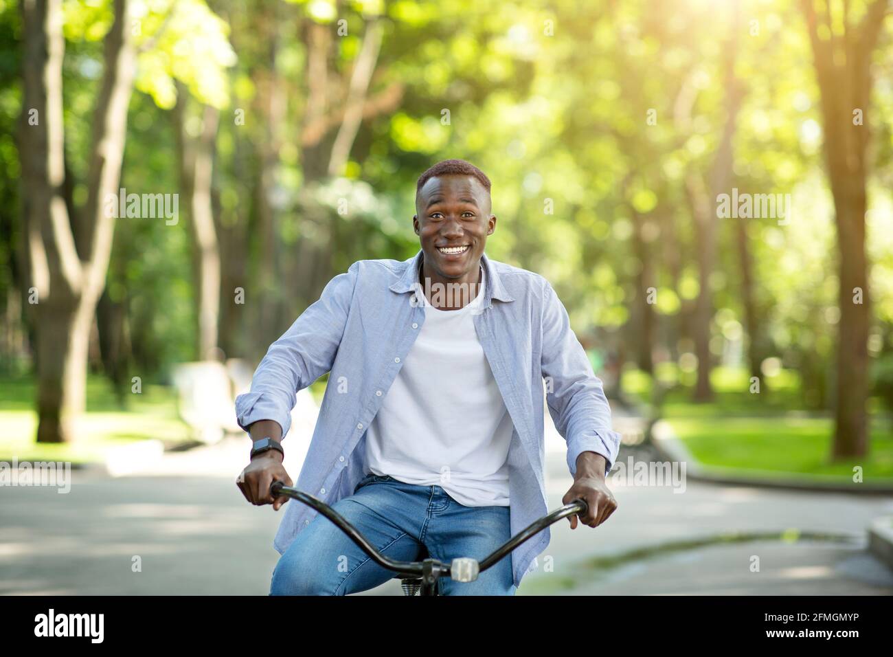 Positive black man having fun riding bike at city park Stock Photo - Alamy