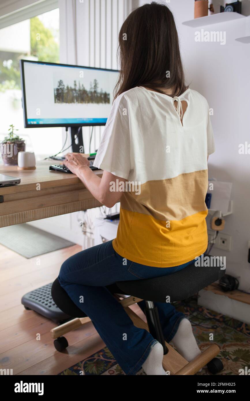 Young woman working at home using an ergonomic kneeling chair seen from ...