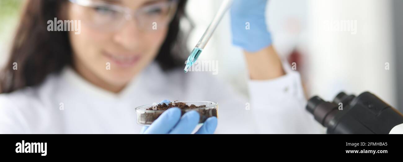 Female scientist dripping liquid from pipette into petri dish with soil ...