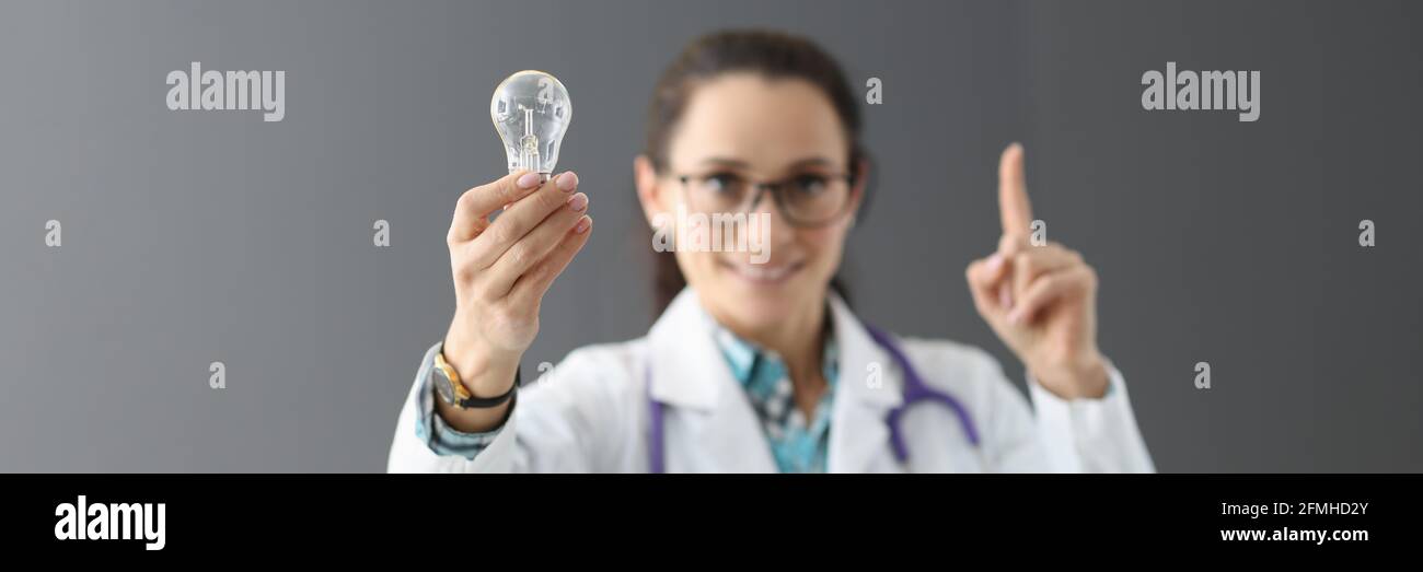 Woman doctor holding light bulb in hands and showing index finger up ...