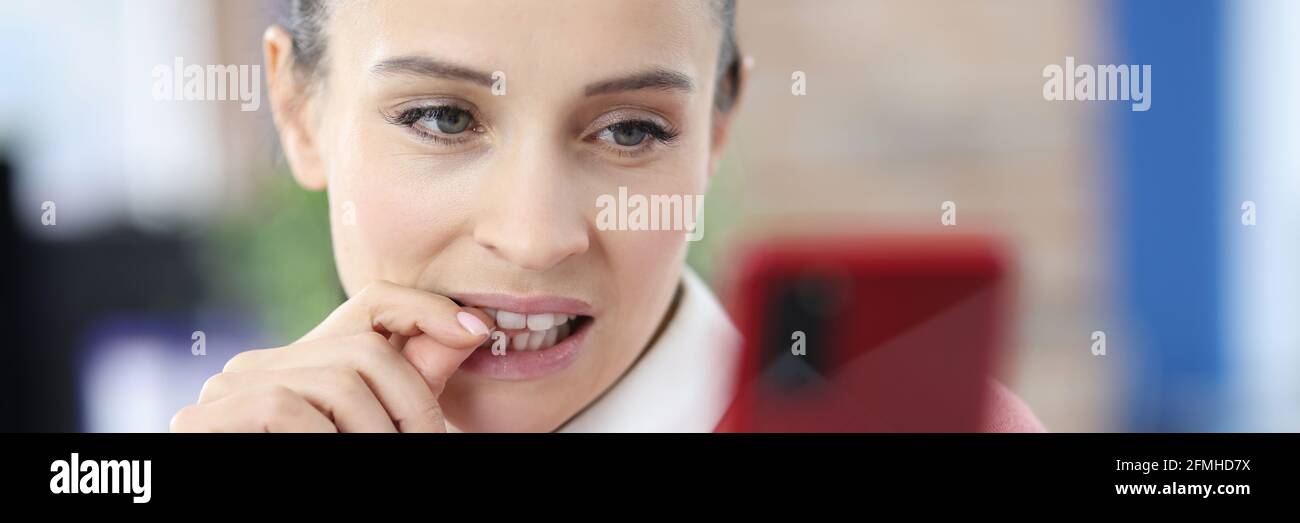 Young woman biting her nails looking at phone screen Stock Photo - Alamy