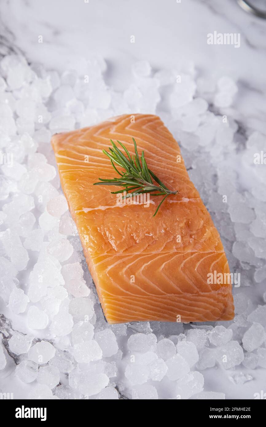 A vertical shot of salmon fillet with a sprig of rosemary on ice on a ...