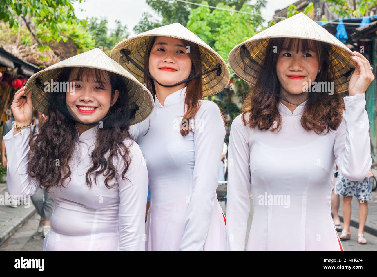 Three Vietnamese women wearing conical hats and dressed in traditional ao dai clothing, Hoi An ...