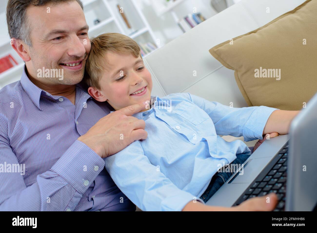 Young boy using laptop, man tickling his chin Stock Photo - Alamy