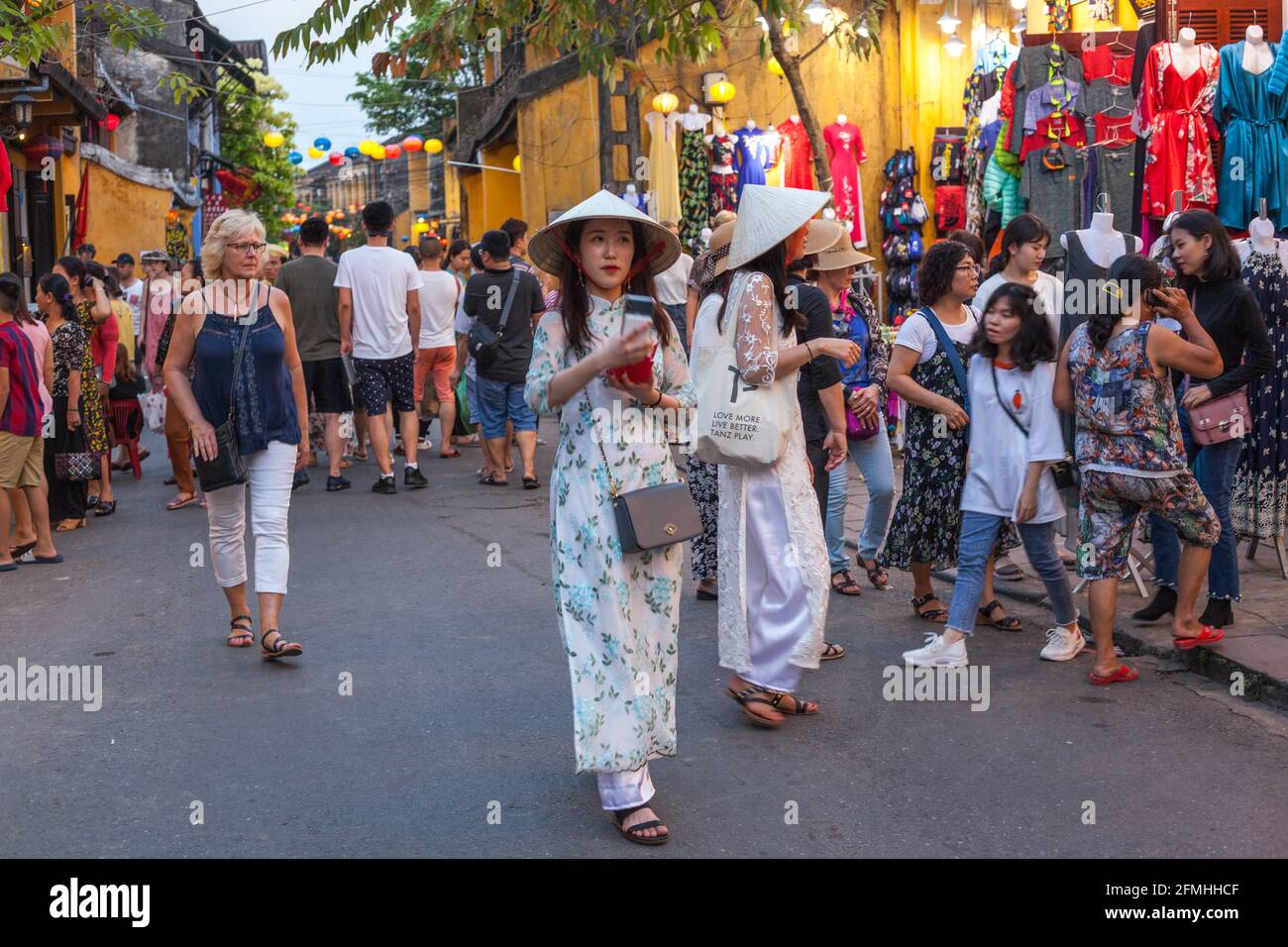 Young Vietnamese women dressed in traditional conical hats and ao dai traditional dresses walk ...