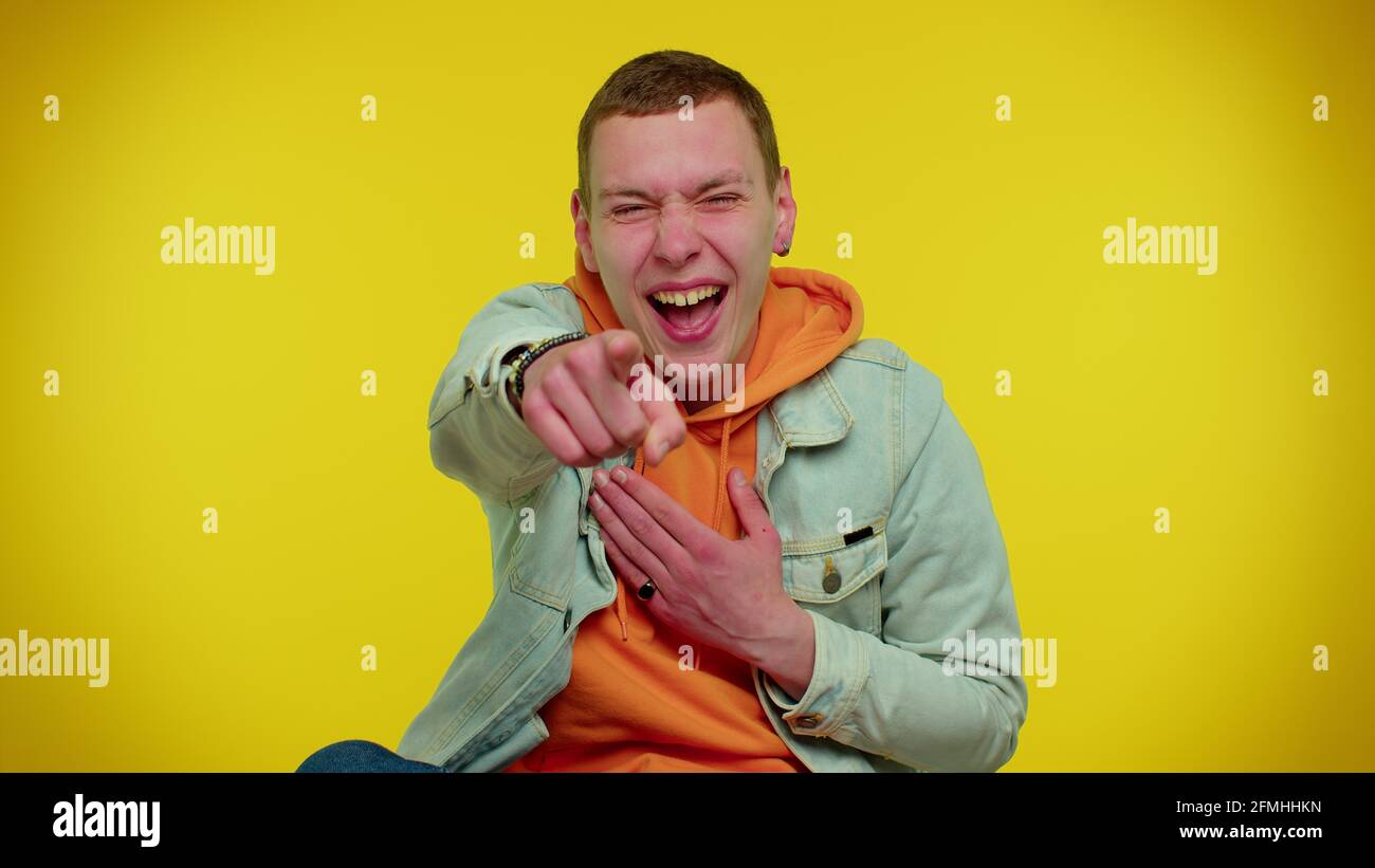 Amused teen stylish man in denim jacket pointing finger to camera ...