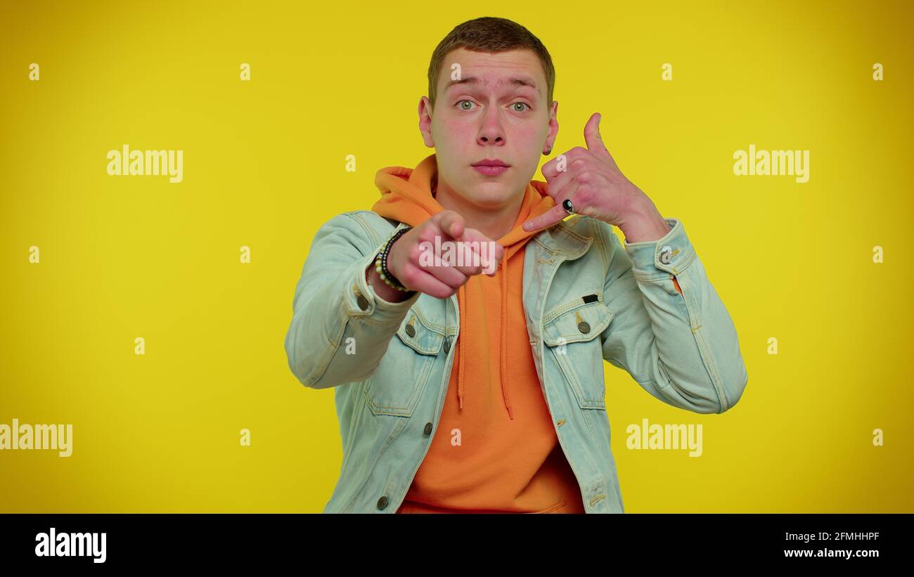 Teenager man in denim jacket looking at camera doing phone gesture like ...