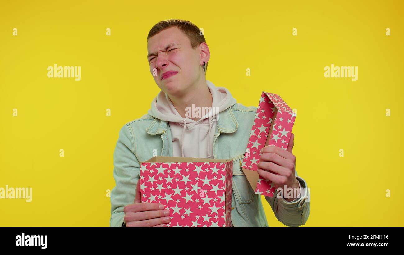 Young man unwrapping birthday gift and expressing disappointment ...