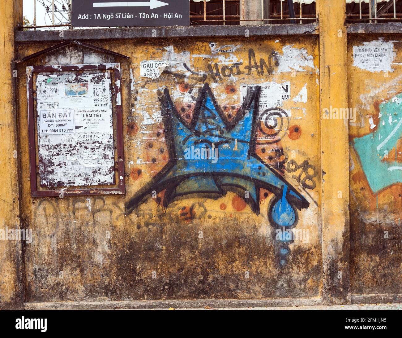 Public notices and spray painted graffiti on yellow wall in Hoi An ...