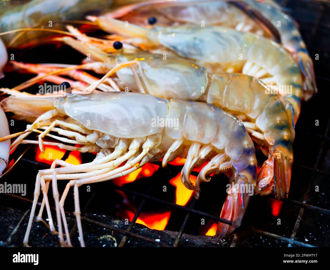 Grilled prawn on flaming grill. Close-up row of raw river prawns are ...