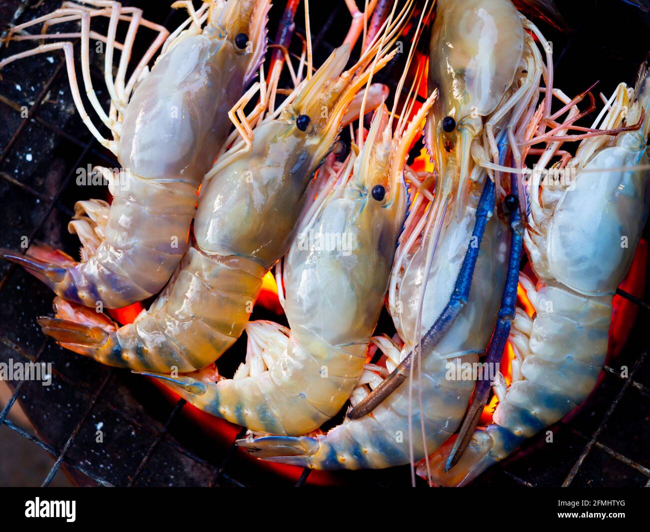 Grilled prawn on flaming grill. Close-up row of raw river prawns are ...