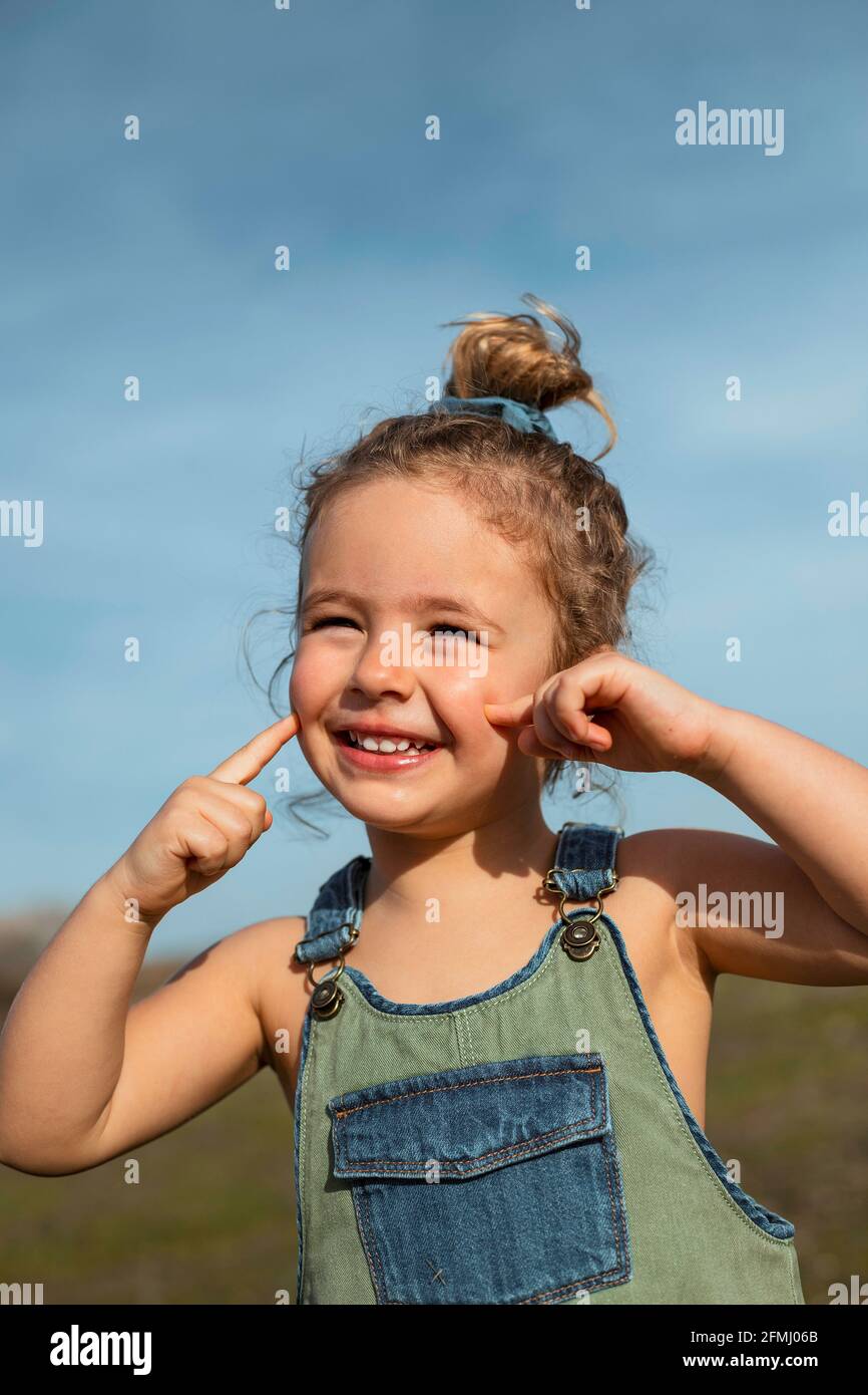 Delighted adorable little girl in overalls standing with fingers on ...