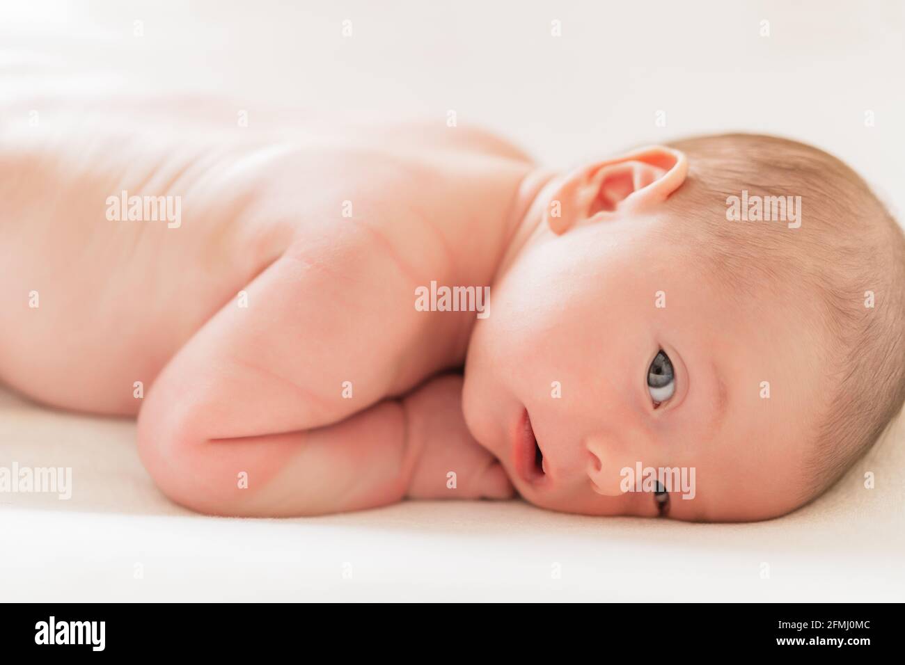 Side view of cute little child looking at camera while lying on textile ...