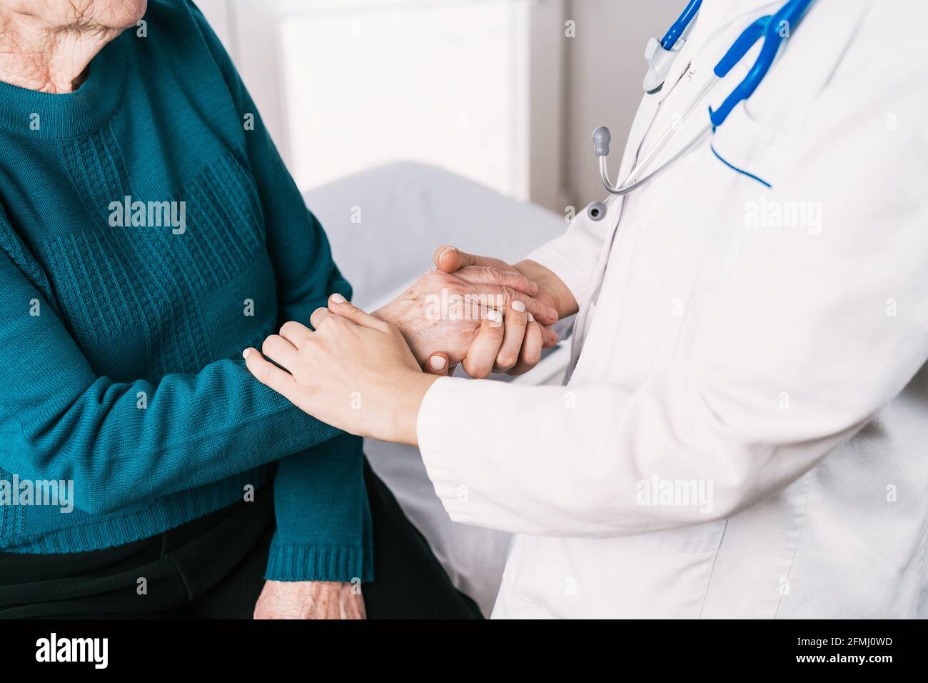 Crop anonymous doctor speaking with elderly Woman while holding hands ...