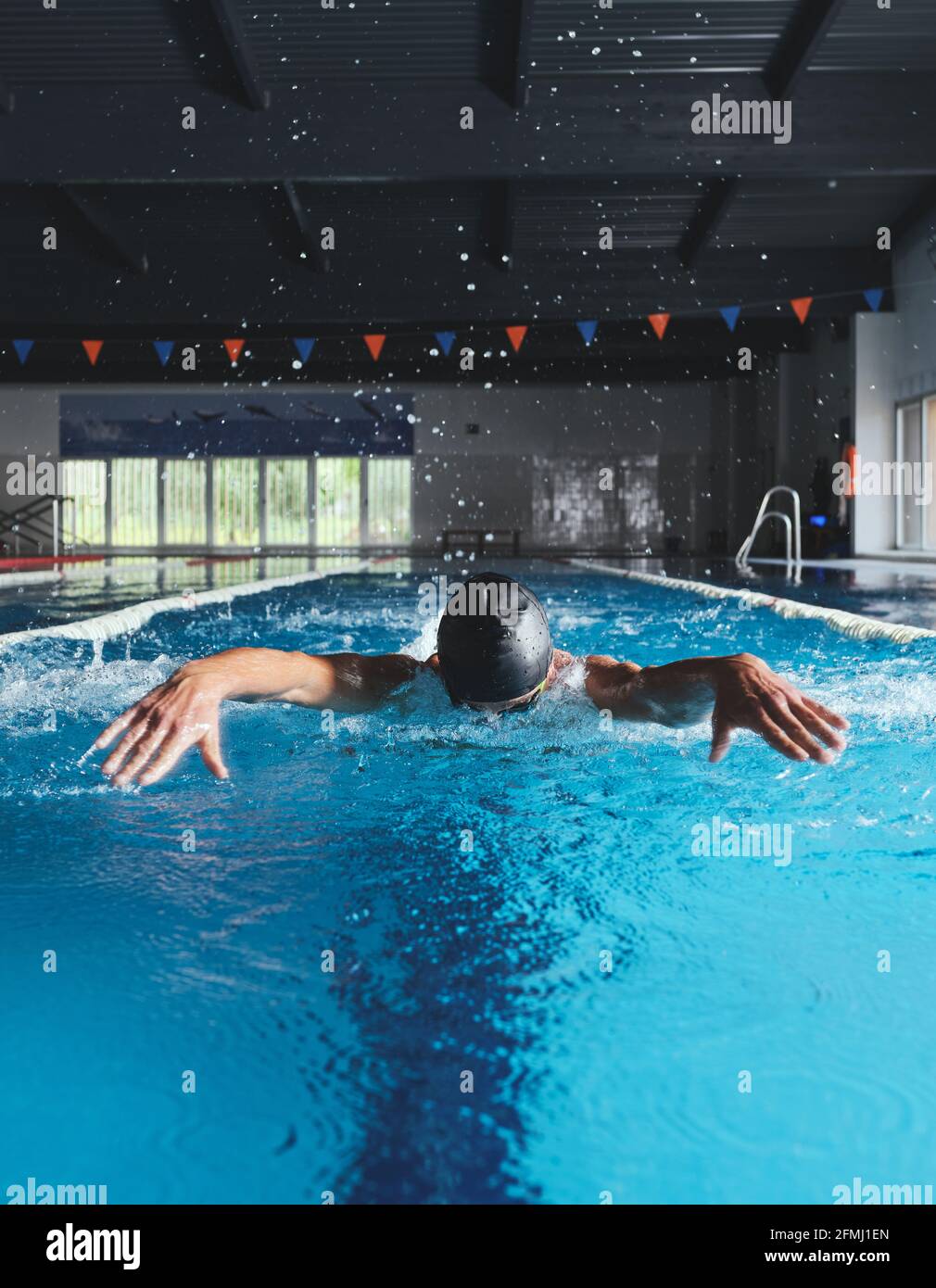 Strong male swimmer in bathing cap performing butterfly stroke during ...