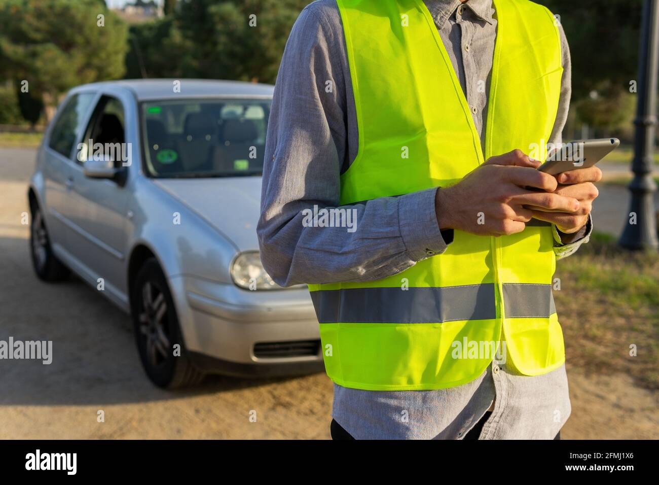 Crop unrecognizable male driver in green safety vest using mobile phone ...