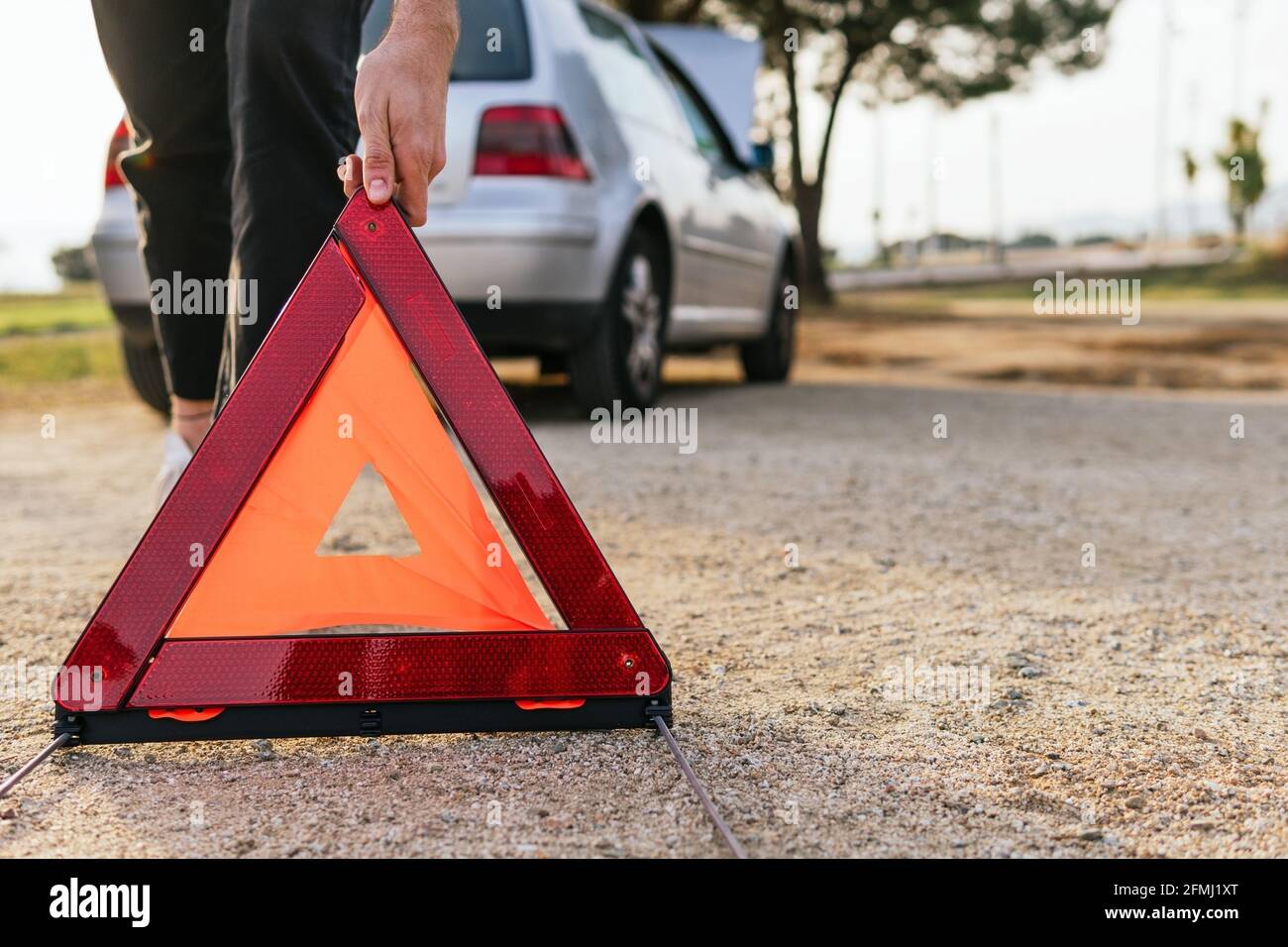 Crop anonymous male driver placing red emergency triangle on country ...