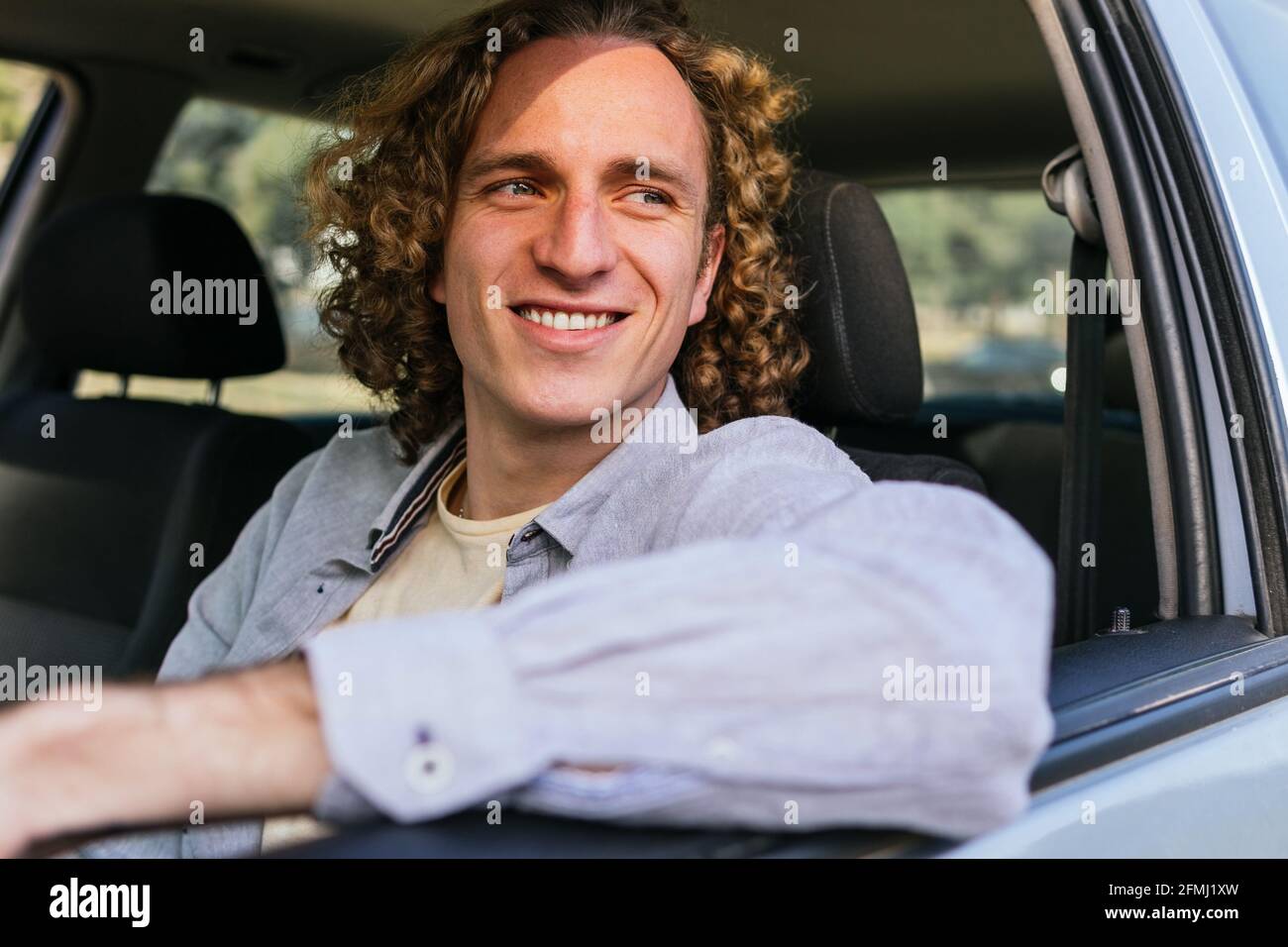 Happy young haired male looking away through open window of car while ...