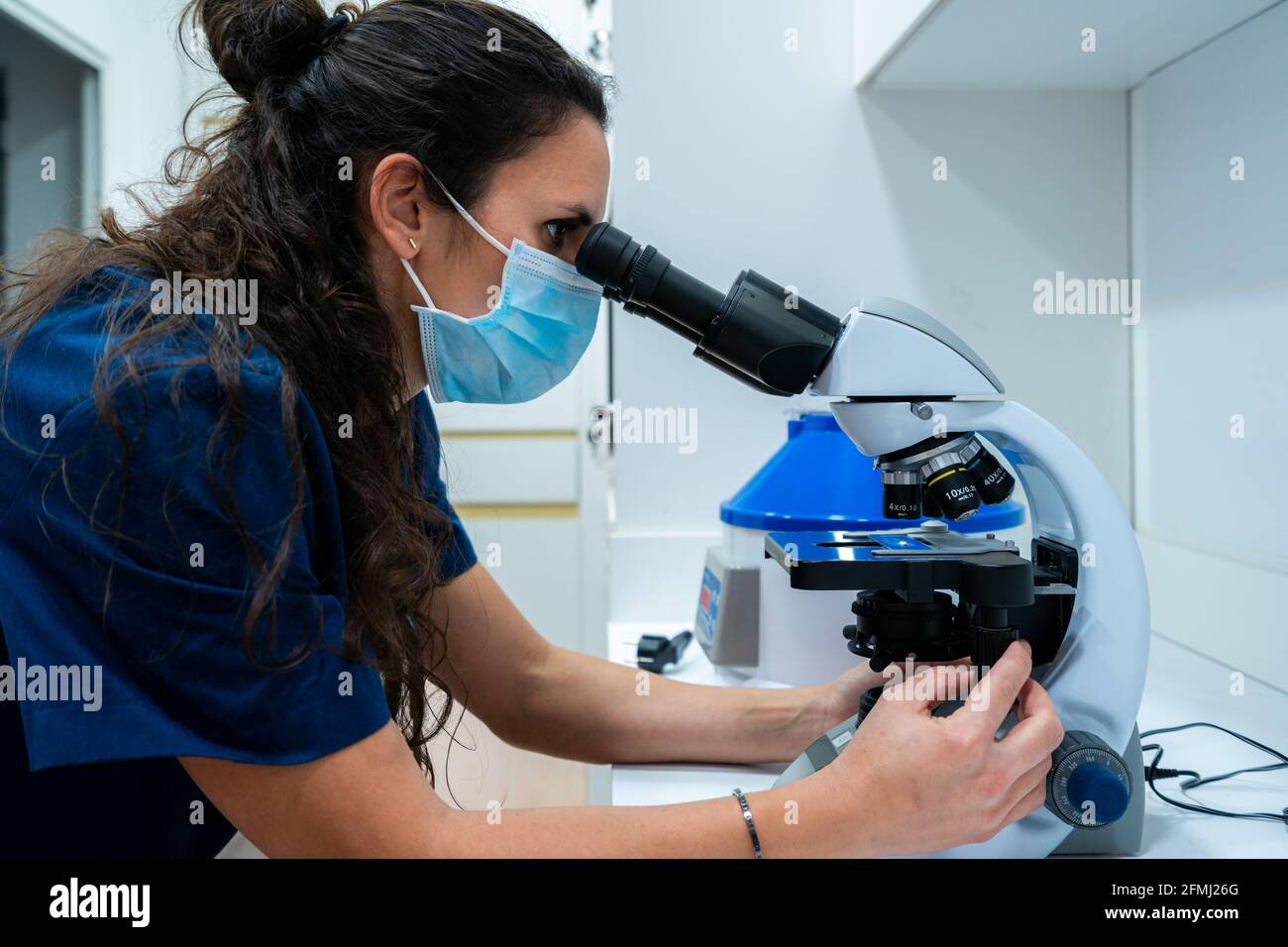 Side view of female vet in blue uniform looking through microscope ...