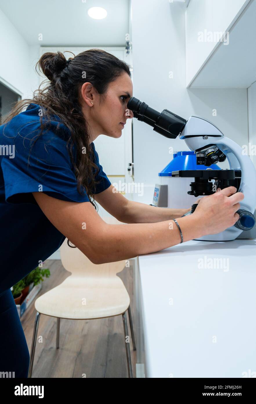 Side view of female vet in blue uniform looking through microscope ...